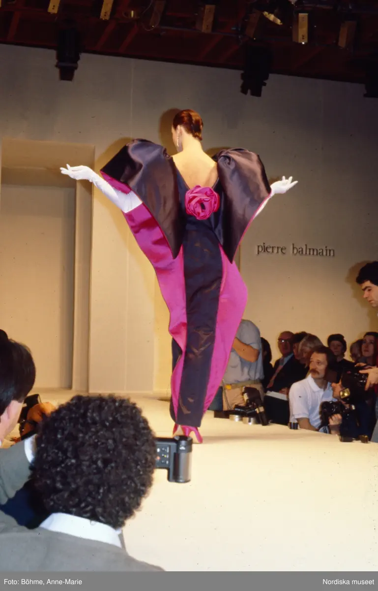 Modevisning. Modell i cerise och mörklila, hellång aftonklänning med ...