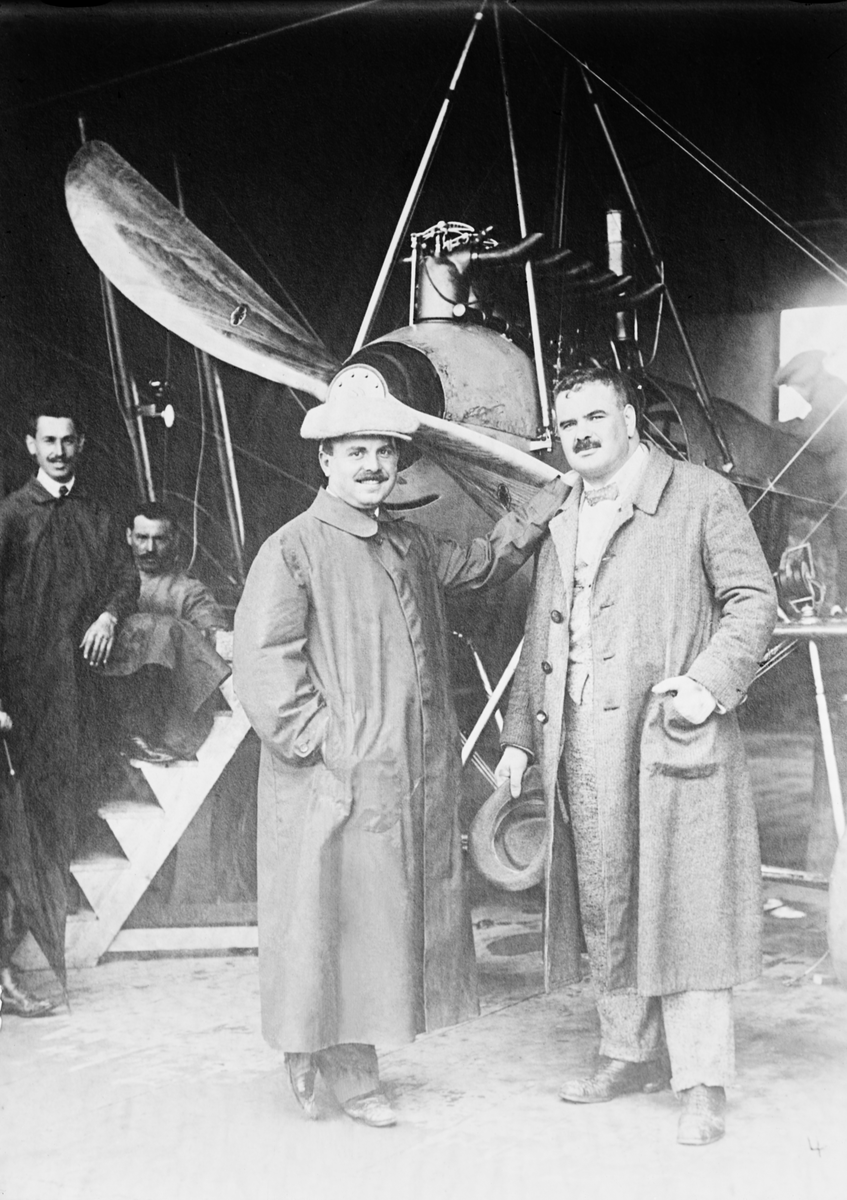 Porträttfoto av två män framför flygplan Lohner B i en hangar. Mannen ...