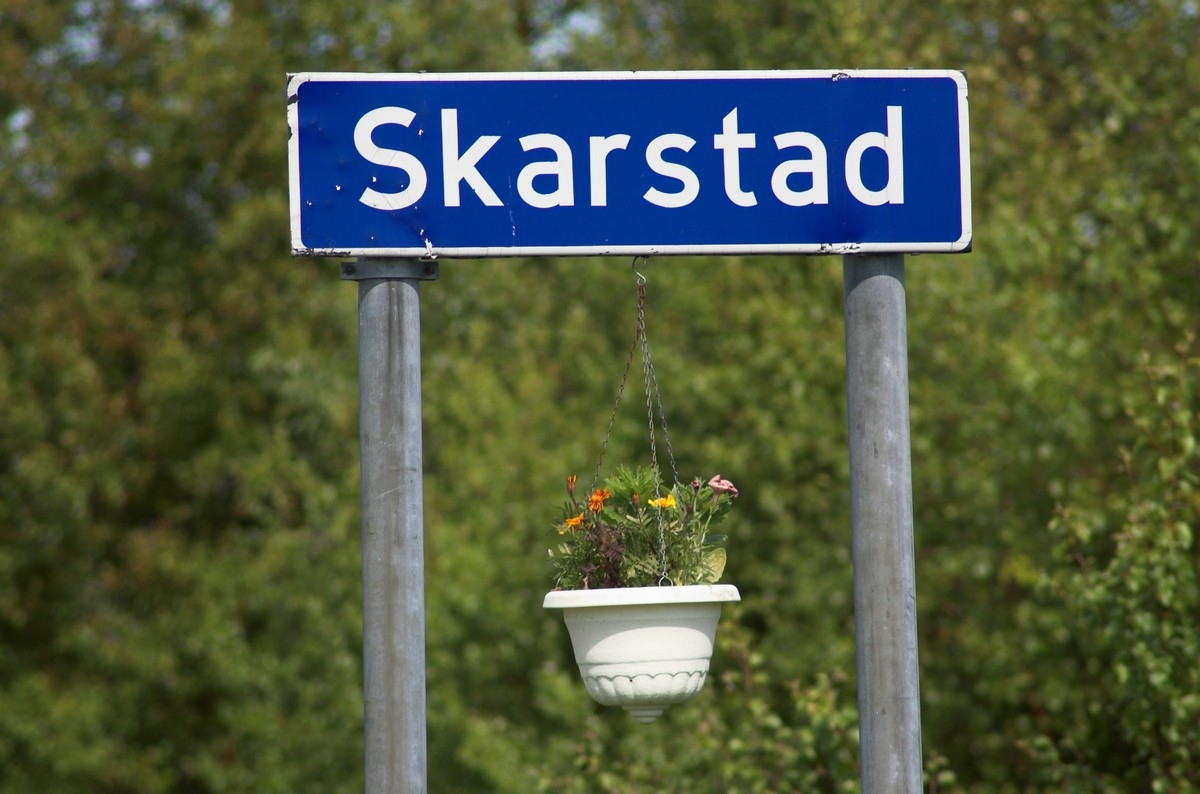 Navneskilt med Skarstad, blomsterpotte henger under. Skilt plassert på ...
