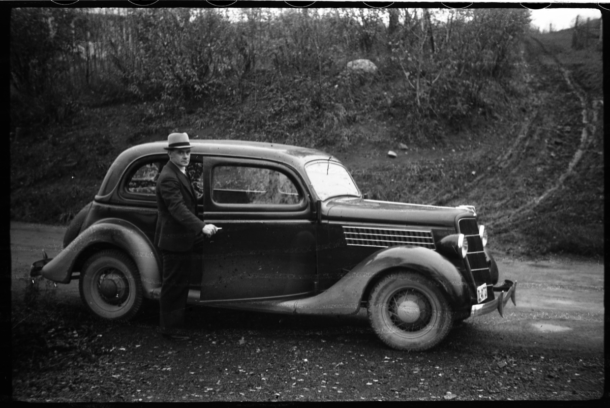 En mann ved navn Øverli, ellers ukjent, fotografert ved siden av en bil ...