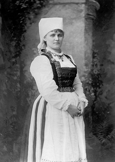 Christina Nilsson i folkdräkt med huckle, hon har halsband och knappar ...