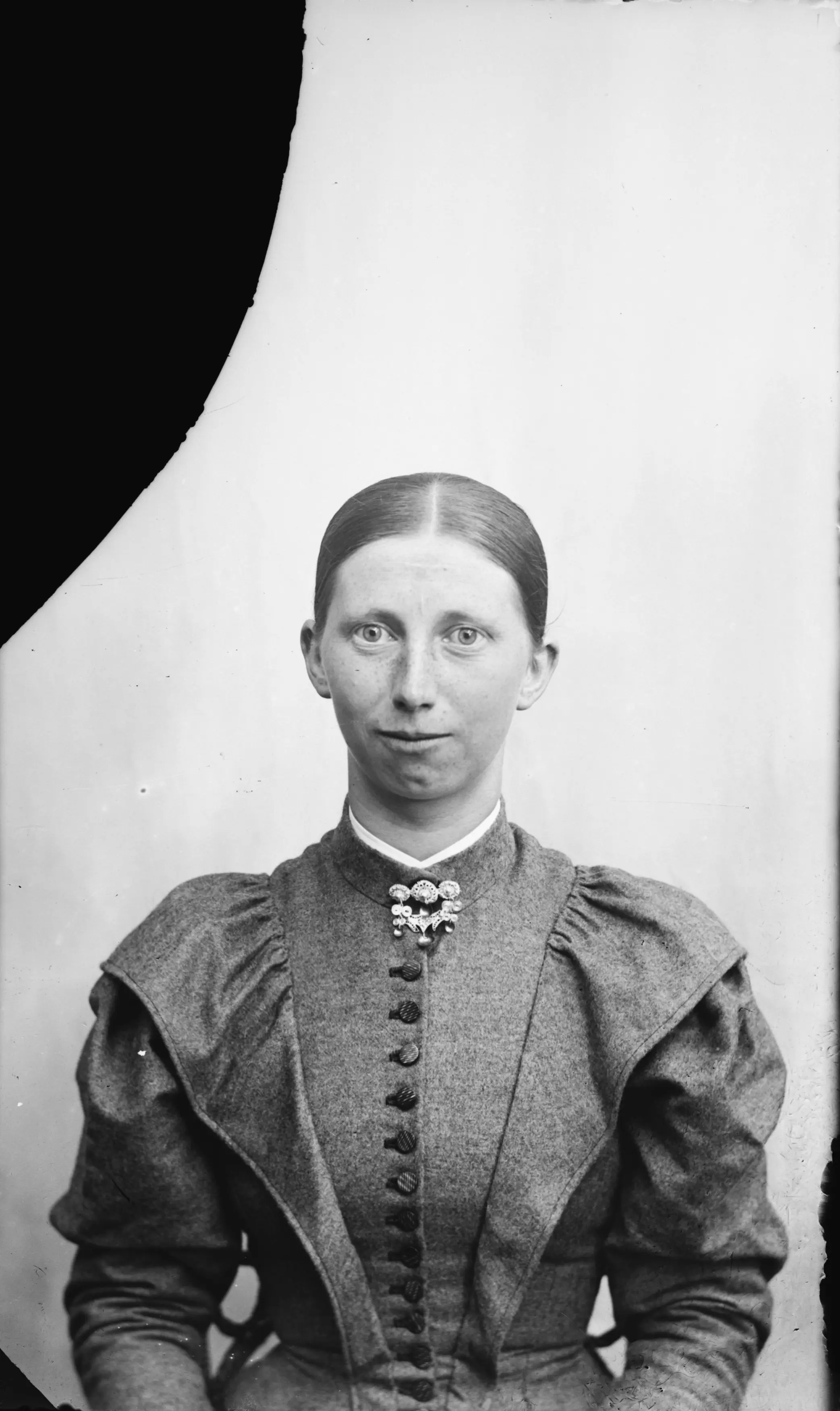 Portrett av kvinne med mørkt hår med midtskille iført kjole med mange ...