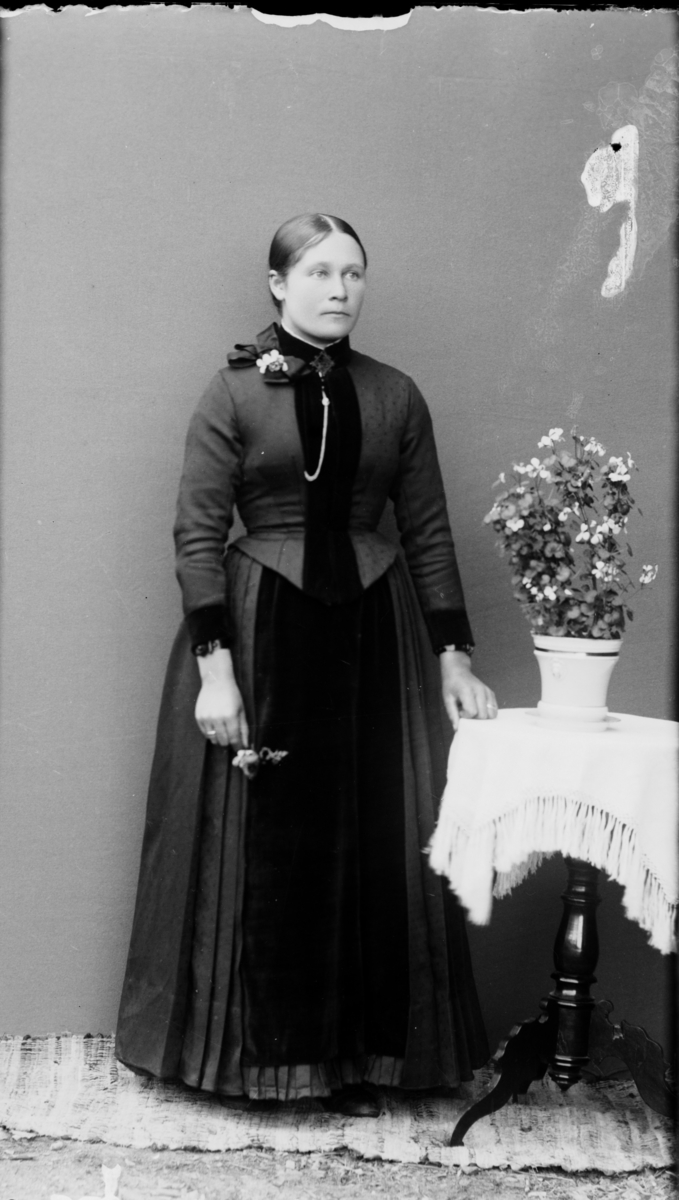 Kvinne med glatt hår med midtskille, kledd i mørk kjole som står ved ...